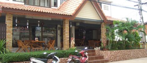 Um edifício com telhado de telhas, uma placa com a inscrição "ROOM BINGALOW" e duas scooters estacionadas na frente.