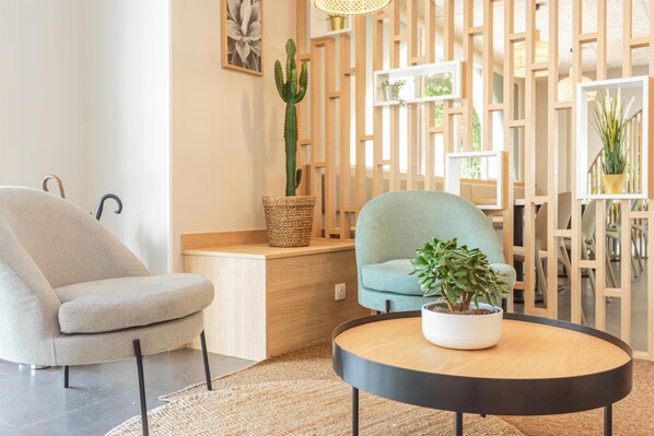 Uma sala de estar moderna com uma poltrona cinza, uma poltrona verde-água, uma mesa de centro redonda de madeira com uma planta em vaso e um painel de madeira com prateleiras.