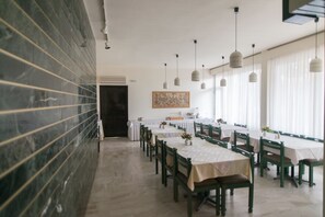 Uma área de refeições com várias mesas e cadeiras, uma parede de mármore e luminárias pendentes.