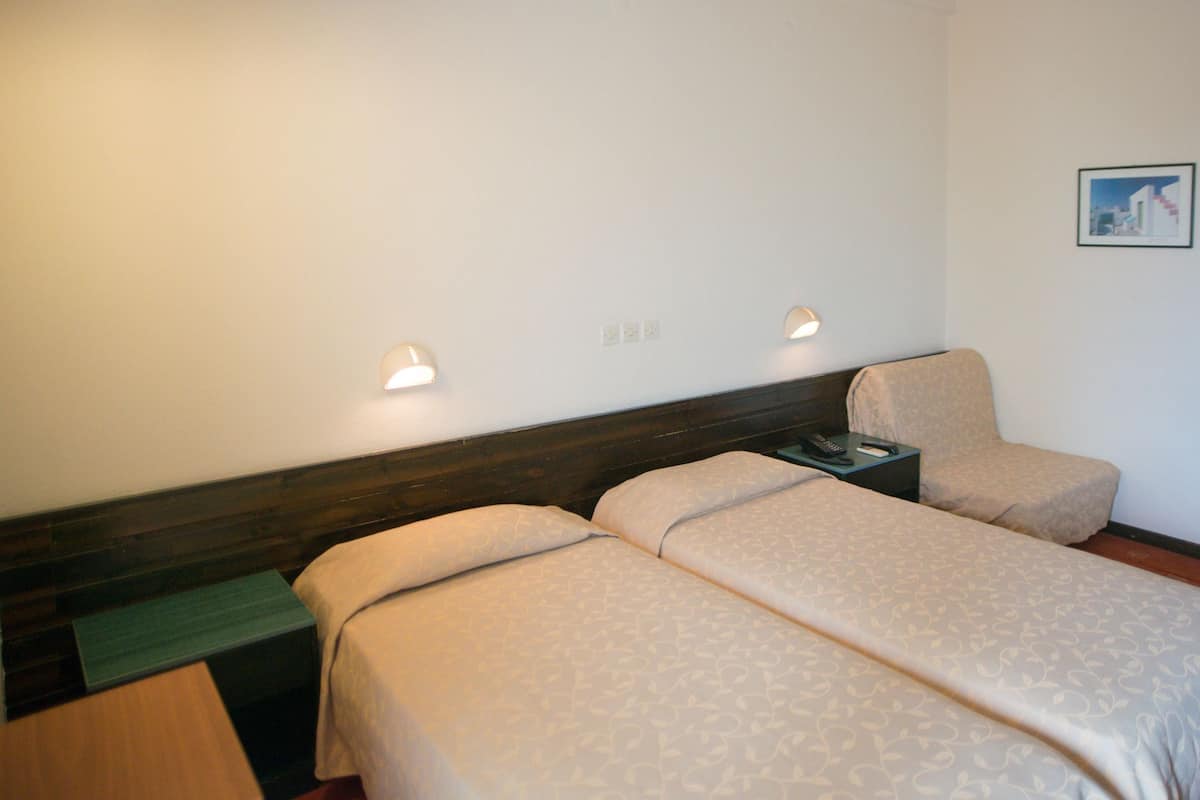 Quarto de hotel com duas camas de solteiro, uma mesinha e um telefone fixado na parede.