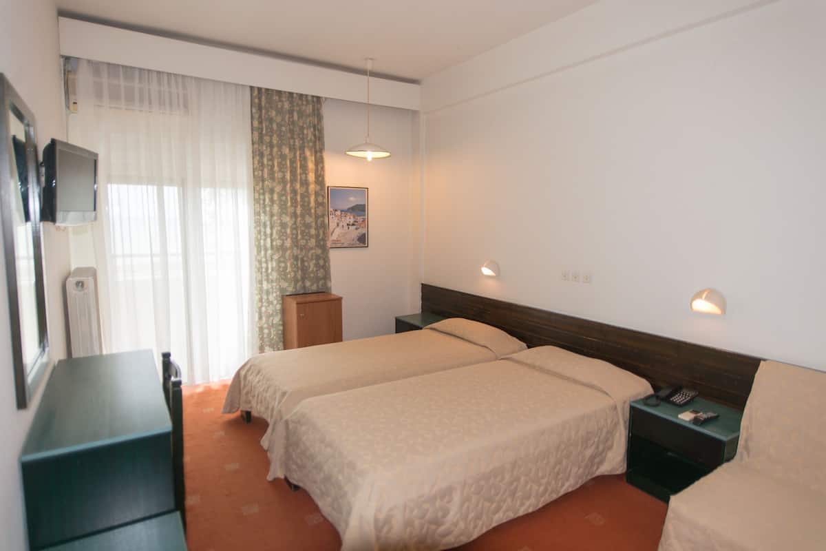 Quarto de hotel com duas camas, uma escrivaninha, uma cadeira, uma televisão e uma janela com cortinas.