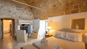 Um quarto aconchegante com parede de pedra, lareira, cama com toalhas dobradas e mesa de cabeceira com abajur.