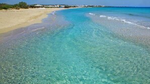 Uma praia com águas turquesa cristalinas, areia dourada e edifícios ao fundo.
