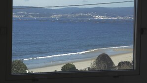 Vista costeira através de uma janela, com praia, oceano e colinas ao longe.