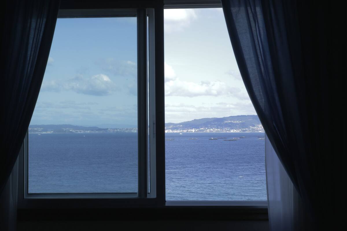 Janela com vista para o mar e terra ao longe.