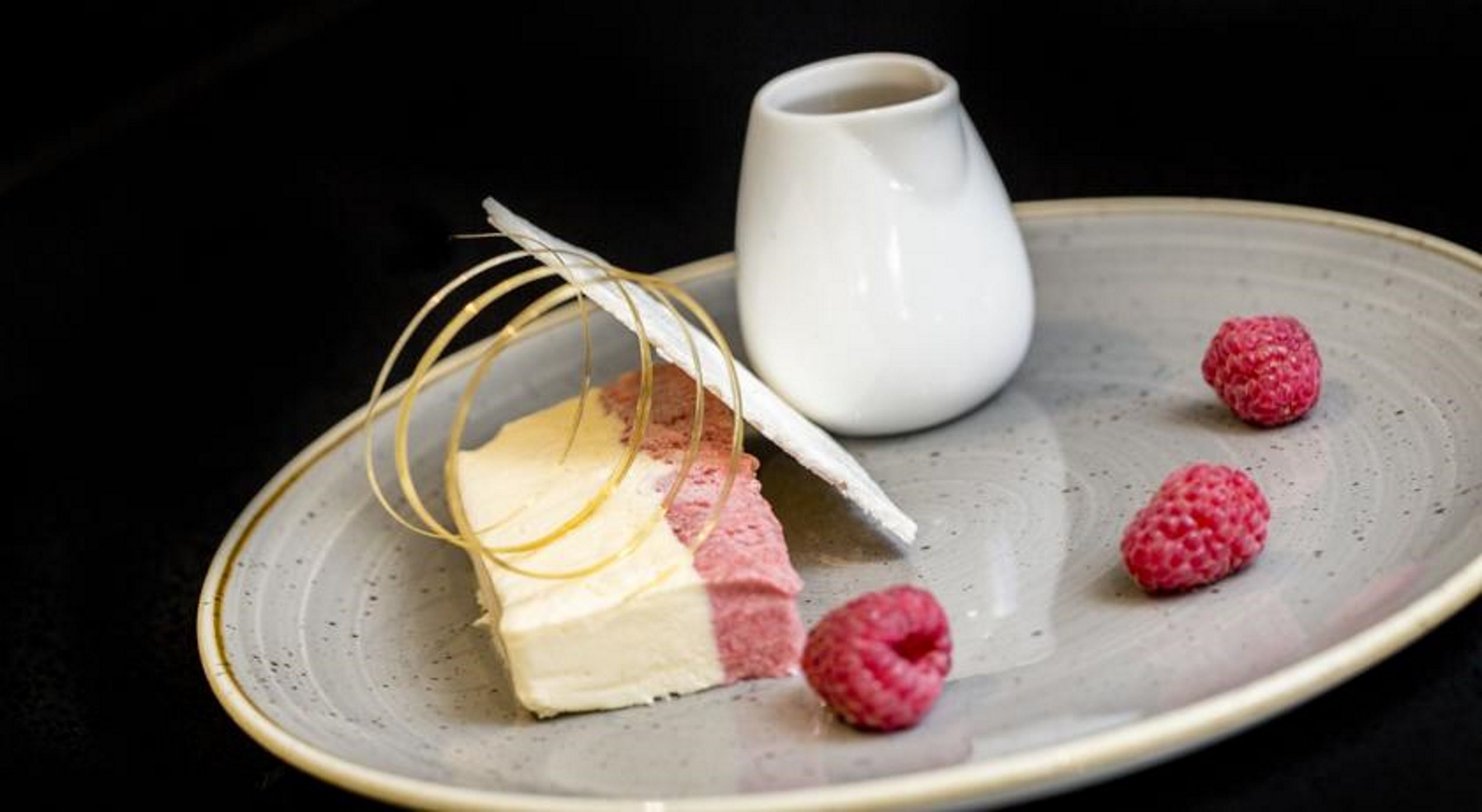 Prato de sobremesa com bolo em camadas, um batedor e um jarro de creme, acompanhados por framboesas.