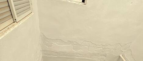 Um pátio pequeno e fechado, com chão de azulejos, uma janela e uma porta.