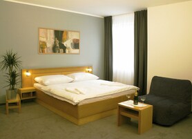 Quarto de hotel com cama, poltrona, mesa pequena, planta e um quadro na parede.
