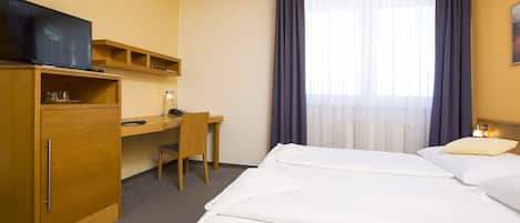 Quarto de hotel com cama, escrivaninha, televisão e guarda-roupa.