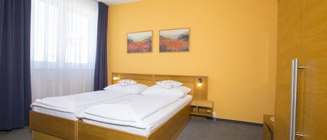 Uma cama de casal com cabeceira de madeira, uma mesinha de cabeceira e duas quadros pendurados na parede.
