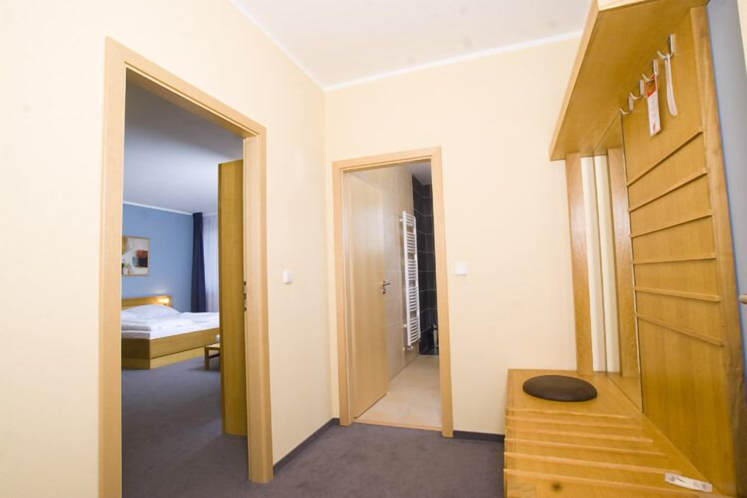 Um corredor estreito com uma cama e um banco de madeira à direita.