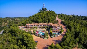 Vista aérea de um resort com vários edifícios, área central com piscina e paisagem arborizada ao redor.