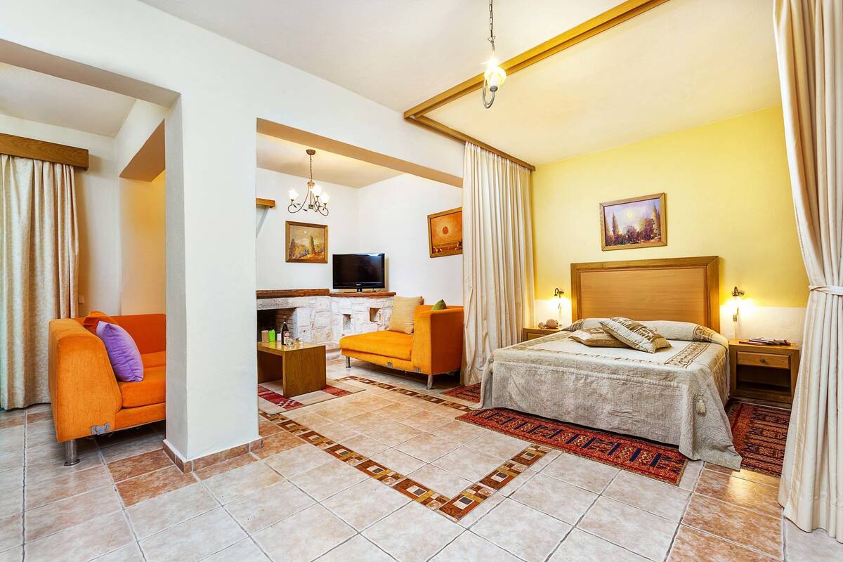 Quarto de hotel com cama, sofá, televisão e pequena cozinha.