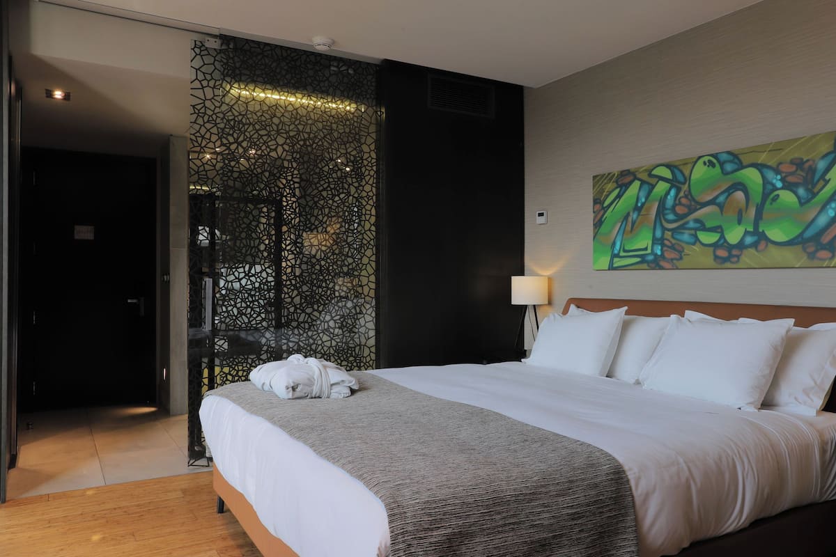 Quarto de hotel moderno com uma cama grande, um painel decorativo na parede e uma pintura abstrata colorida.