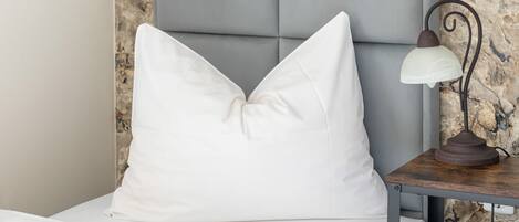 Uma cama com travesseiro branco, mesa de cabeceira com abajur e parede texturizada ao fundo.