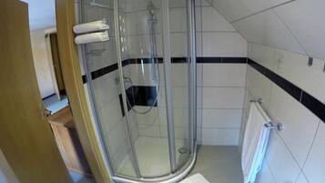 Área de chuveiro com divisória de vidro, porta-toalhas e suporte para papel higiênico.