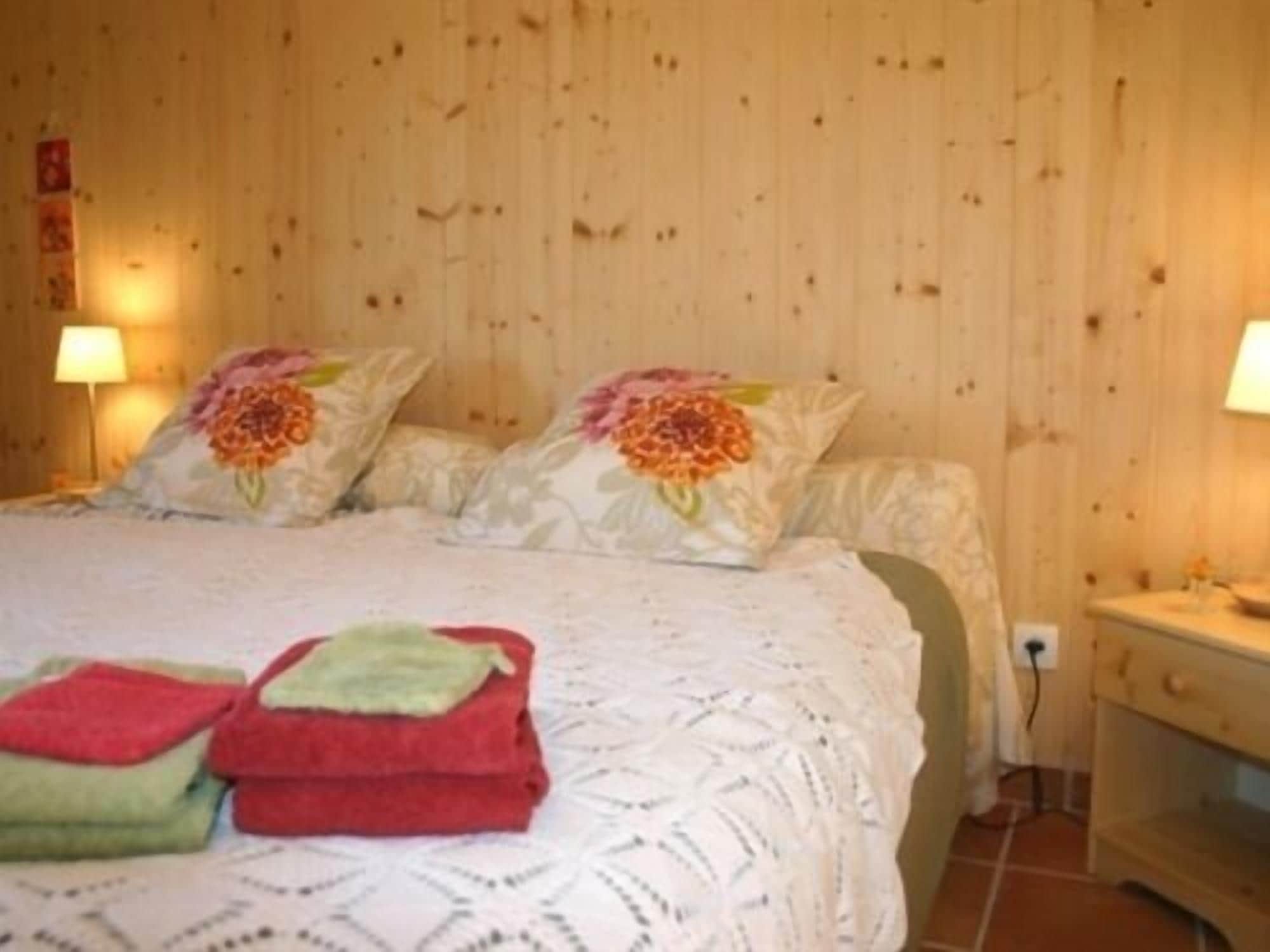 Quarto com painéis de madeira, uma cama, duas luminárias de cabeceira e um criado-mudo.