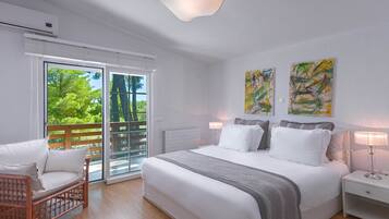 Quarto com uma cama grande, uma cadeira de madeira, mesa de cabeceira e duas pinturas abstratas na parede.