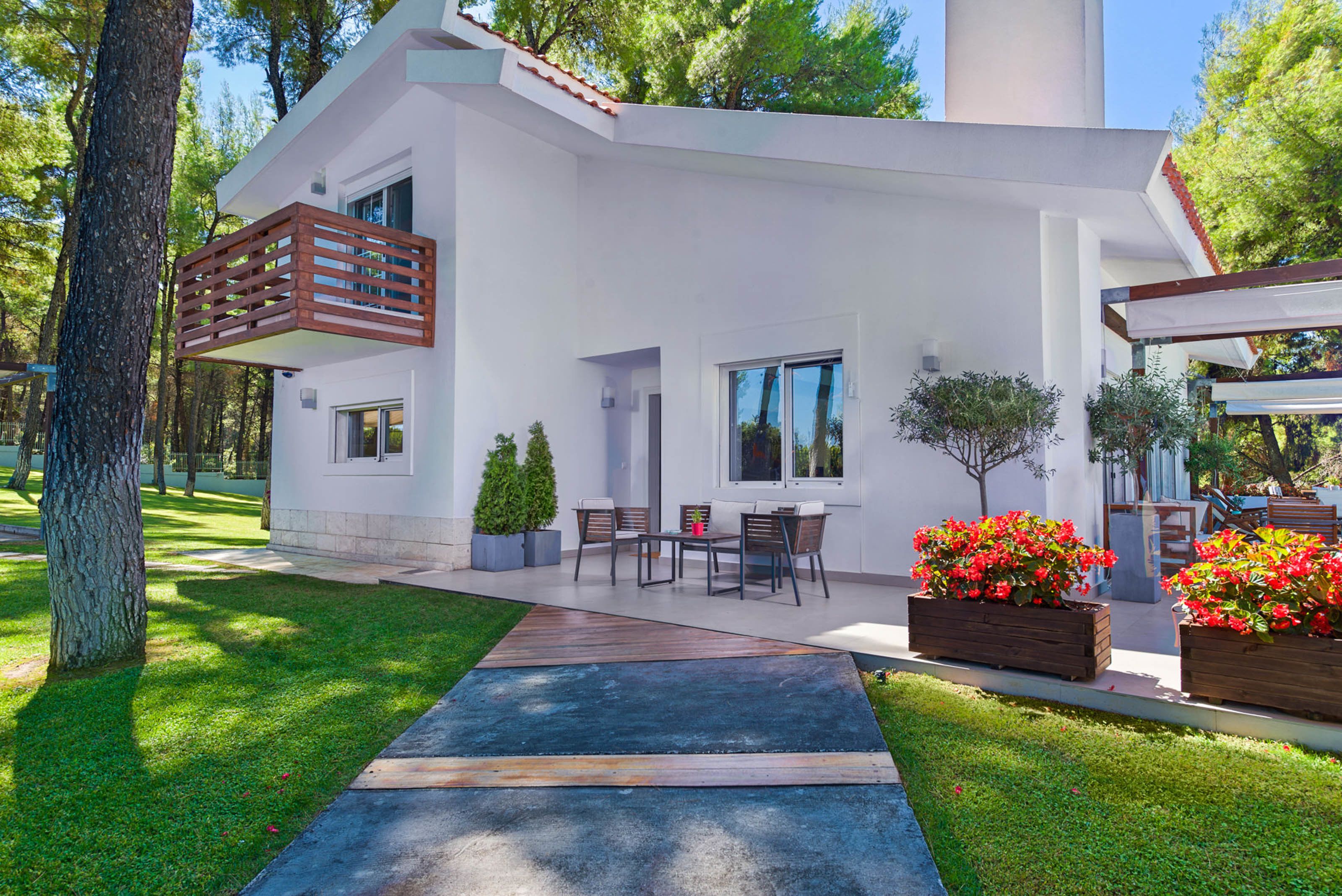 Uma casa moderna com varanda, um pátio com mobiliário de exterior e plantas em vasos.