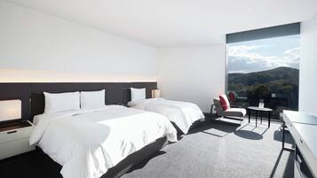 Quarto de hotel moderno com duas camas, uma escrivaninha, uma cadeira e uma janela grande com vista para o exterior.