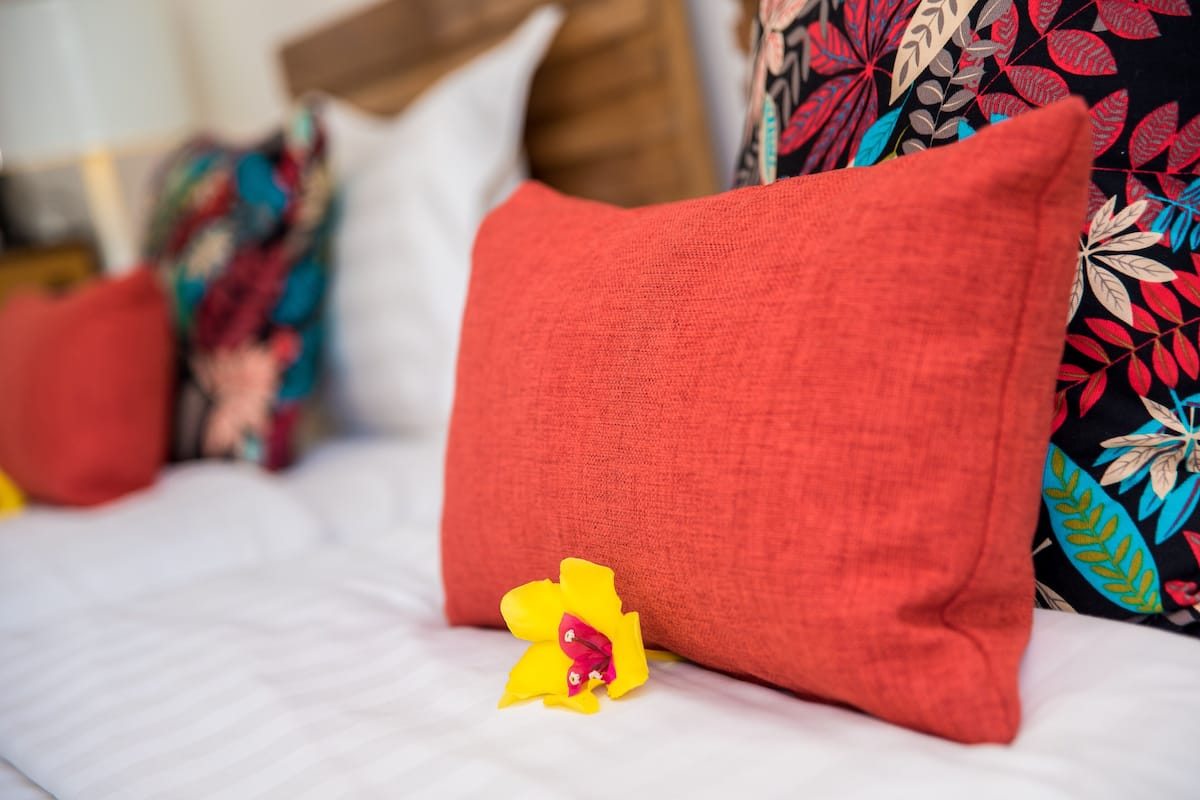 Uma cama com um travesseiro vermelho, um travesseiro branco e um travesseiro colorido com padrão floral.