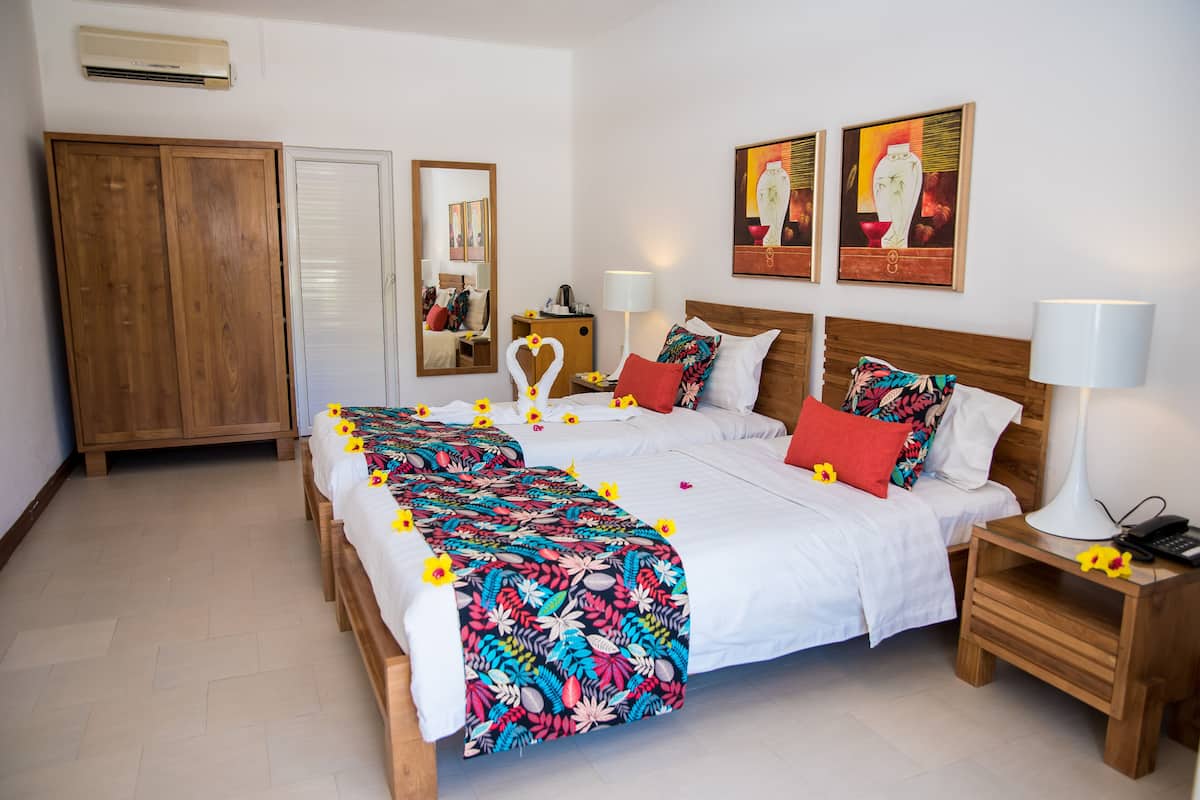 Quarto de hotel com duas camas, um guarda-roupa, um espelho e obras de arte na parede.
