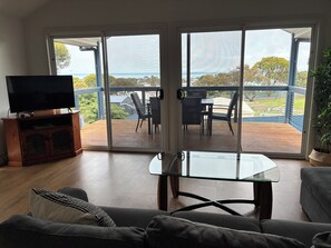 Uma sala de estar com televisão, mesa de centro de vidro e sofá.