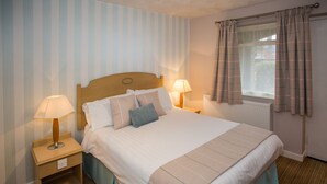 Cama bem arrumada com cabeceira de madeira, duas luminárias de apoio e uma janela com cortinas.