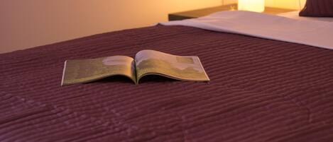 Uma cama com um livro, uma luminária de cabeceira e um travesseiro.