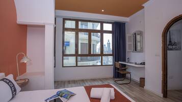 Quarto de hotel com cama, escrivaninha, cadeira, janela com vista para edifícios e espelho com imagem da Torre Eiffel.