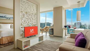 Quarto de hotel moderno com cama, televisão, área de estar e vista para a cidade.