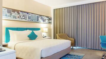 Quarto de hotel com cama, uma cadeira, escrivaninha com abajur e vista para a cidade.