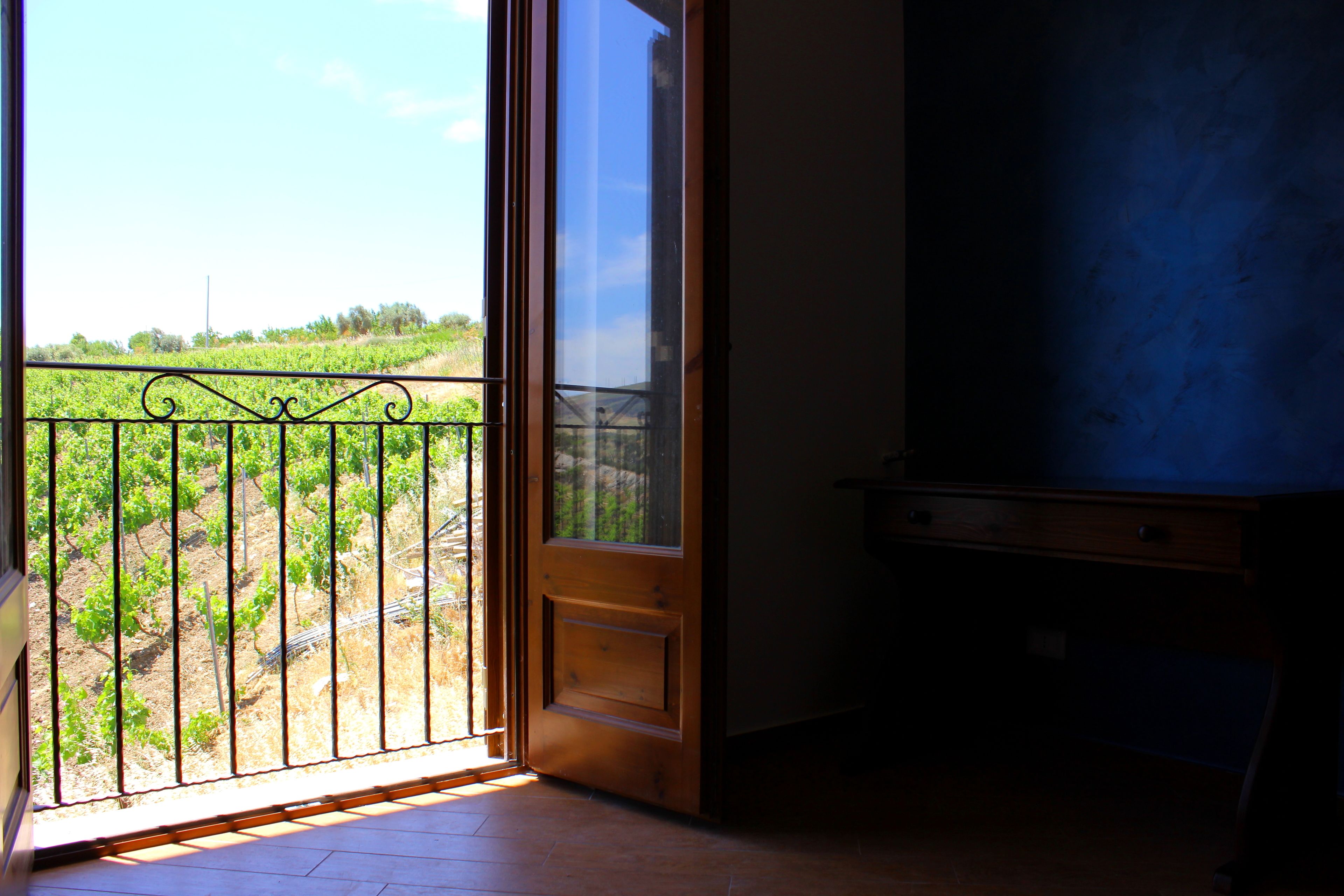 Quarto com uma grande janela, uma escrivaninha de madeira e vista para um vinhedo.