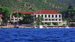 Um edifício costeiro com telhado vermelho, localizado à beira-mar com barcos ancorados por perto.