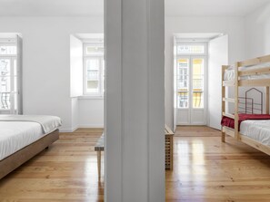 Quarto com duas camas, piso de madeira, paredes brancas e janela com vista para uma varanda.