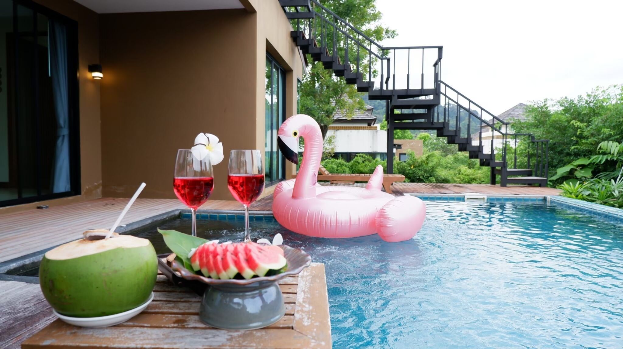 Uma área de piscina com boia de flamingo, bebidas e melancia.