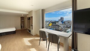 Quarto de hotel moderno com uma janela grande, televisão de tela plana, área de refeições e uma pequena cozinha.