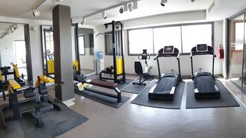 Academia com equipamentos de ginástica, esteiras e uma grande janela.