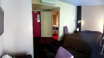 Quarto de hotel com uma cama, uma TV, uma escrivaninha e uma cadeira.