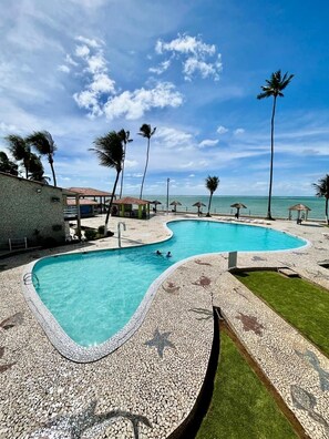 Piscina com design curvo, rodeada por um deck de pedra e palmeiras.