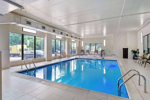 Uma piscina interior com janelas amplas, chão revestido de azulejos e algumas cadeiras de descanso.