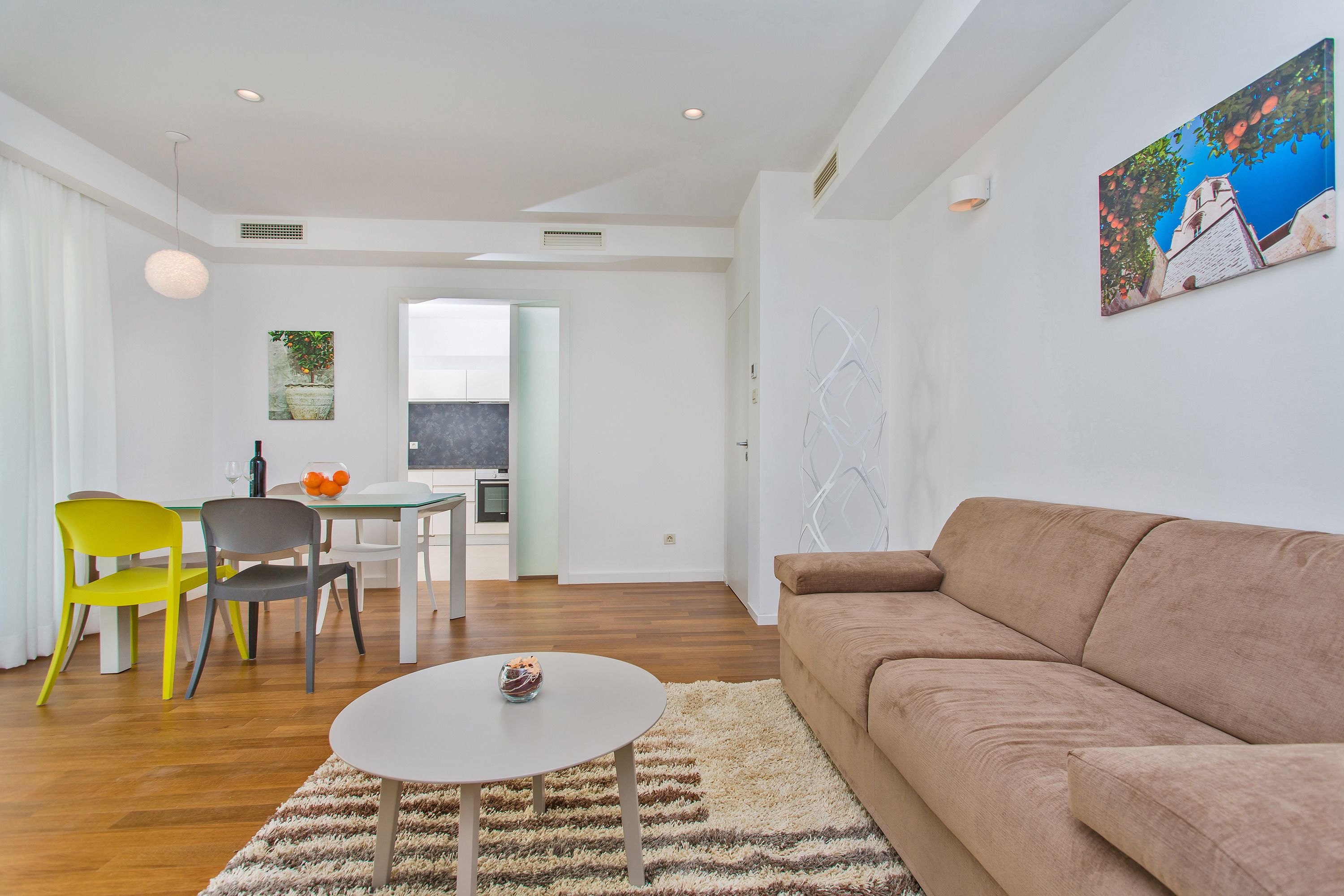 Uma sala de estar moderna com um sofá, uma mesa de jantar com cadeiras e uma cozinha ao fundo.