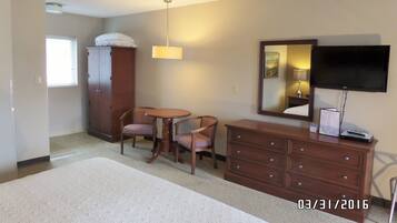 Quarto de hotel com cama, cómoda de madeira, televisão, secretária com duas cadeiras e guarda-roupa.