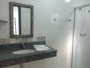 Casa de banho com lavatório de granito, espelho, toalha e chuveiro com porta de vidro.