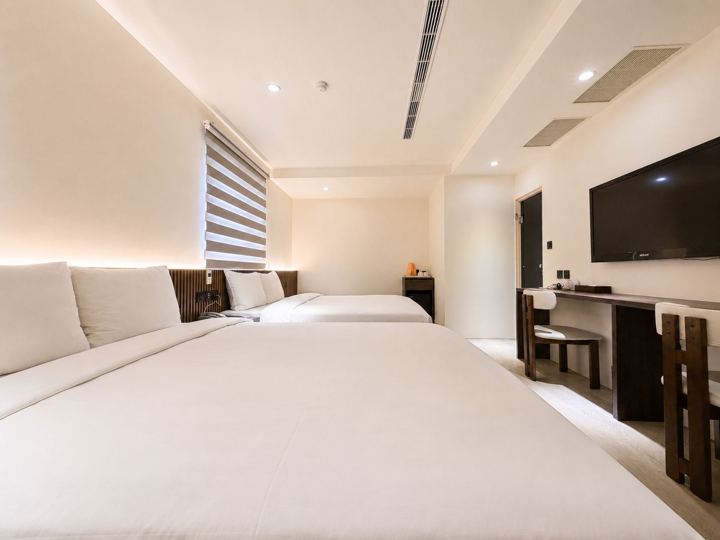 Quarto de hotel com duas camas, televisão, escrivaninha e uma cadeira.
