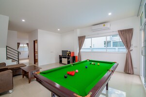 Uma mesa de bilhar com bolas, um sofá, uma televisão e uma janela com cortinas.