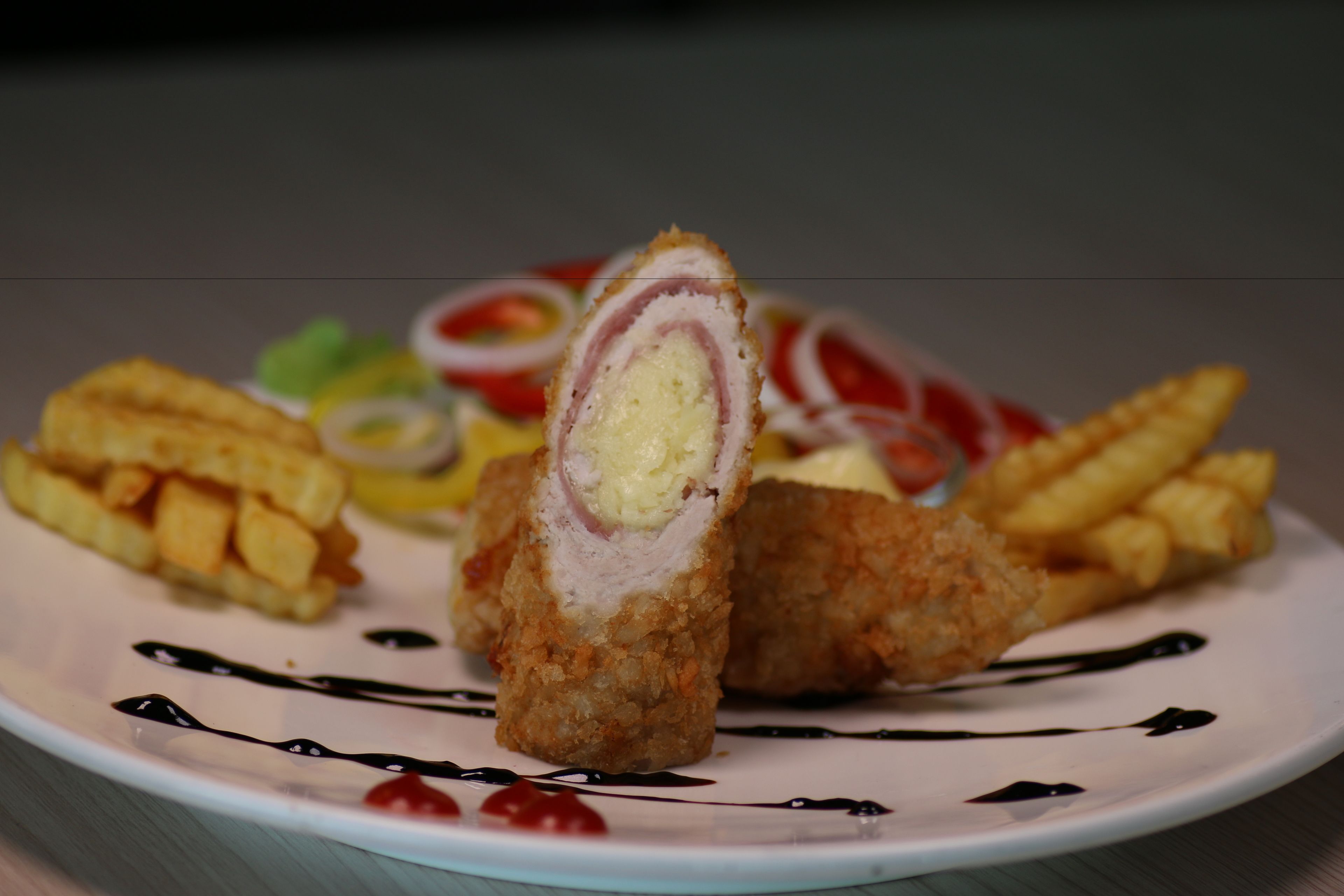 Um prato com um alimento empanado e frito, possivelmente frango, acompanhado de batatas fritas e cebola fatiada.