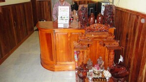 Balcão de recepção com acabamento em madeira, um aviso e vários objetos decorativos, incluindo figurines e um vaso.