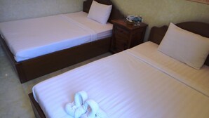 Duas camas de casal com lençóis brancos, uma cabeceira de madeira e uma mesa de cabeceira com uma luminária e uma garrafa.