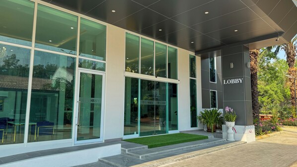 Um edifício moderno com grandes janelas de vidro, uma placa com a palavra 'Lobby' e um jardim bem cuidado.